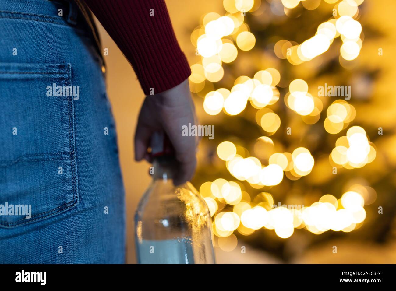 Person in front of the Christmas tree with a bottle of alcohol ...
