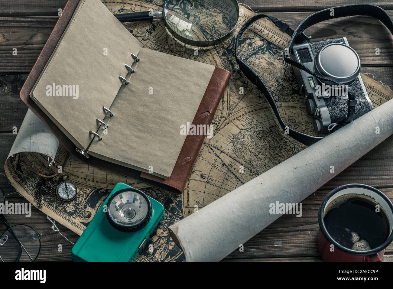 A map spread out on the table with a cup of hot tea and useful items ...