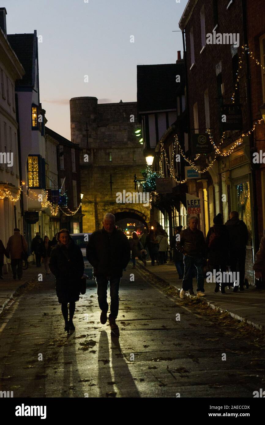 Shoppers walking down a medieval street lined with Christmas lights ...