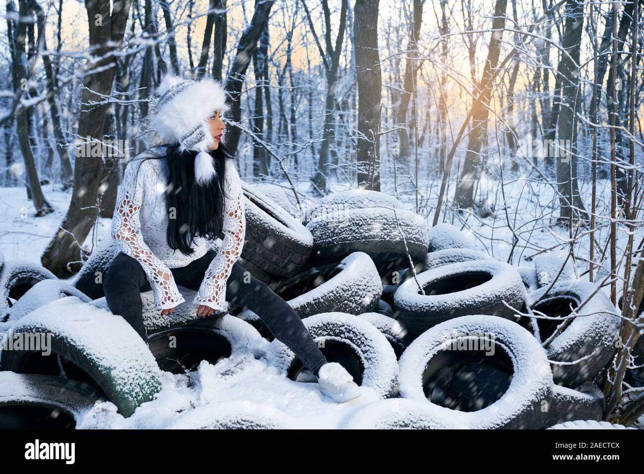 Beautiful girl sitting on old used tires covered with snow dumped in ...