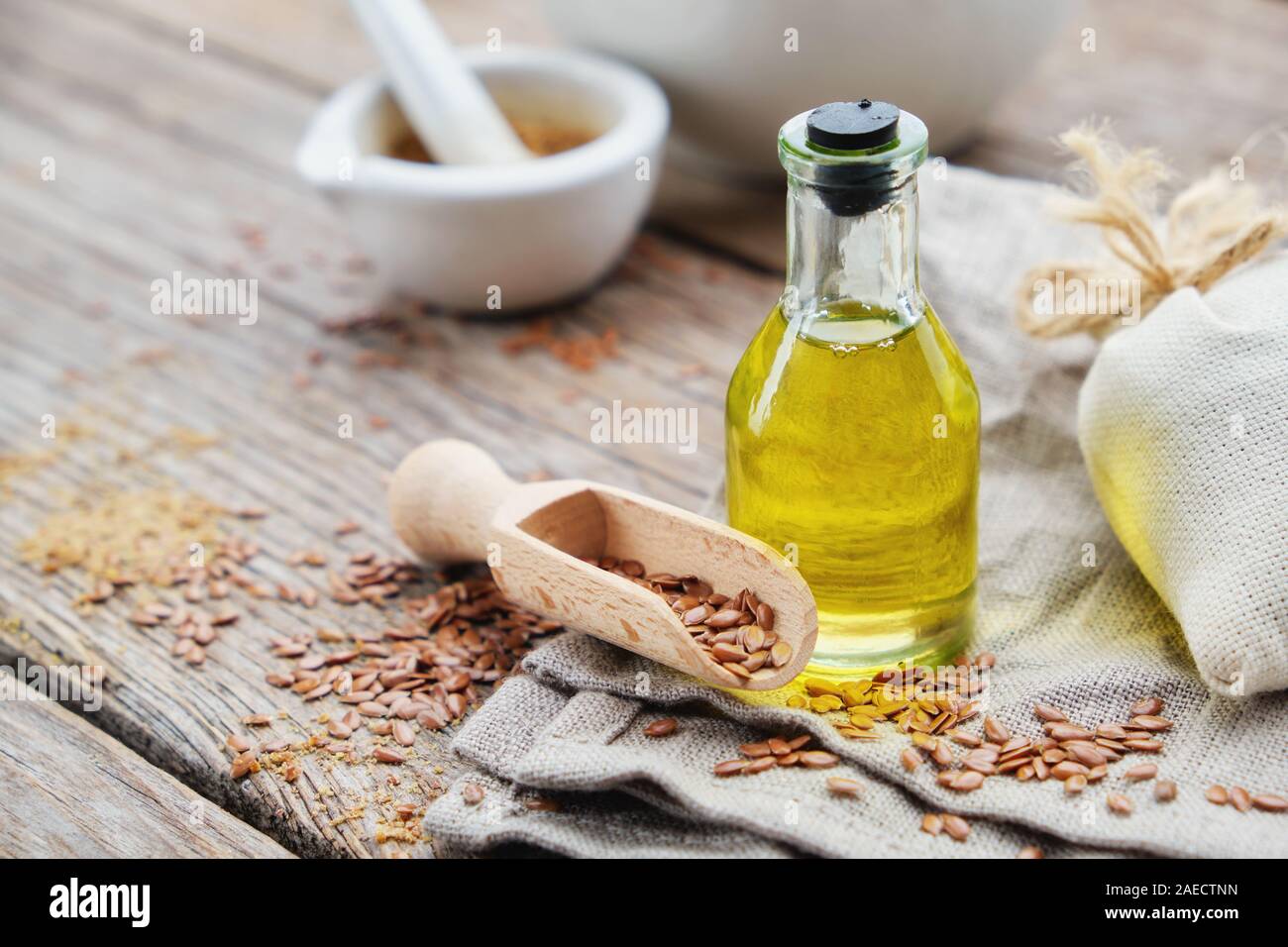 Bottle of fresh linseed oil, wooden scoop of flax seeds on linen cloth. Mortar on background ...