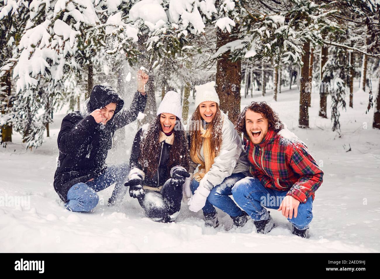 A group of friends under a tree with falling snow in a park in winter ...