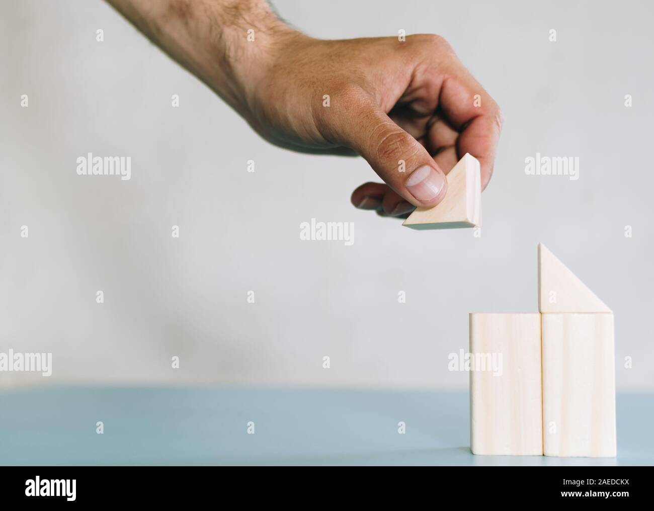 part of human hand while building house from natural color wooden block ...