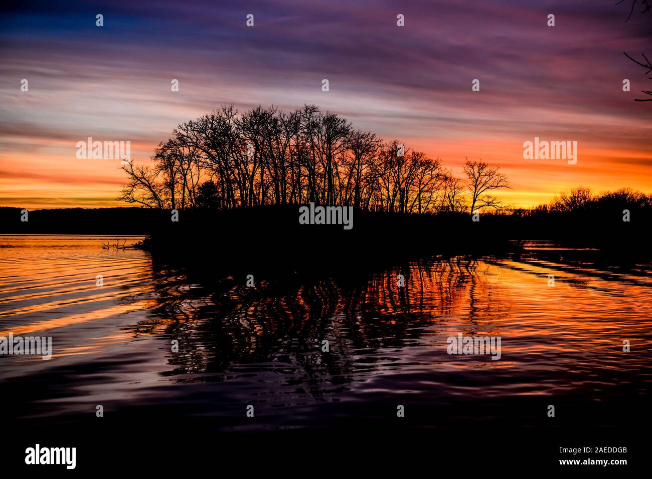 A sunset-illuminated sky behind an island within a lake. The small ...