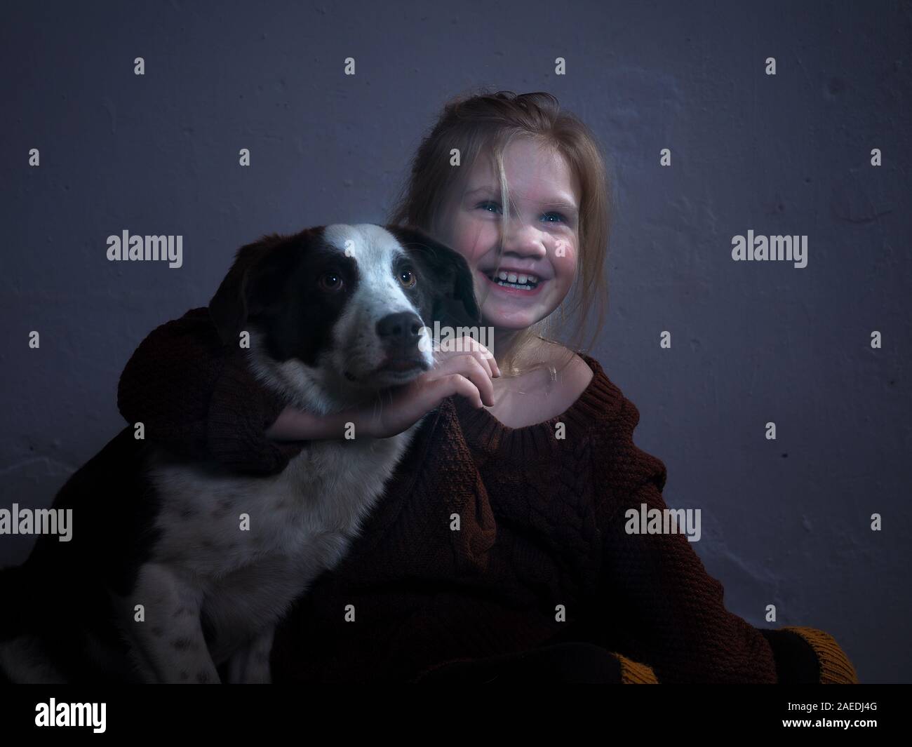 A child and a dog are watching TV in the dark. The light from the ...