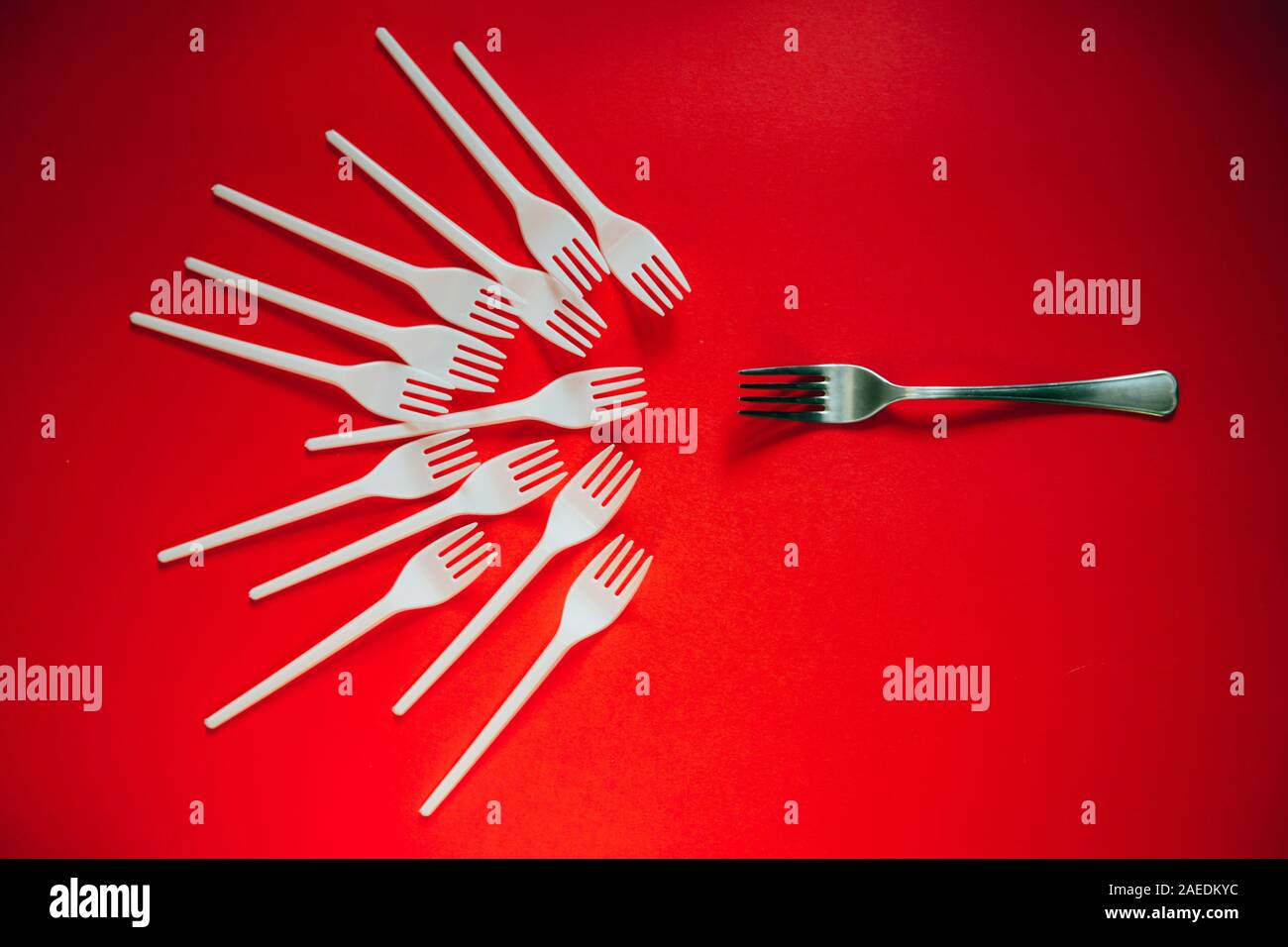 A lot of plastic forks vs one metal on a red background. The concept of ...