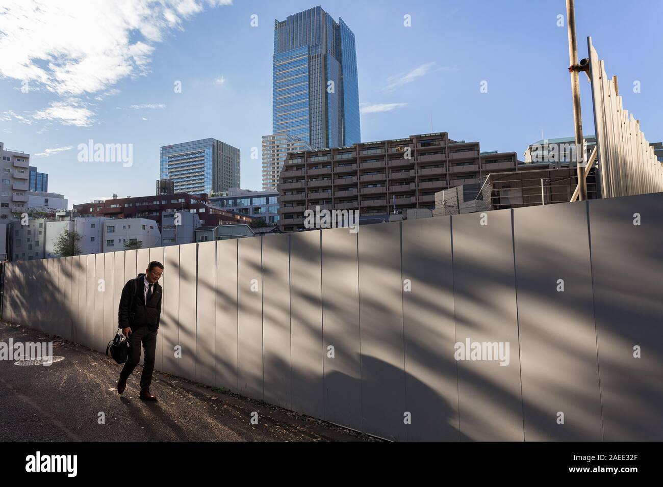 A Japanese salaryman walks by a construction site wall with the tower ...
