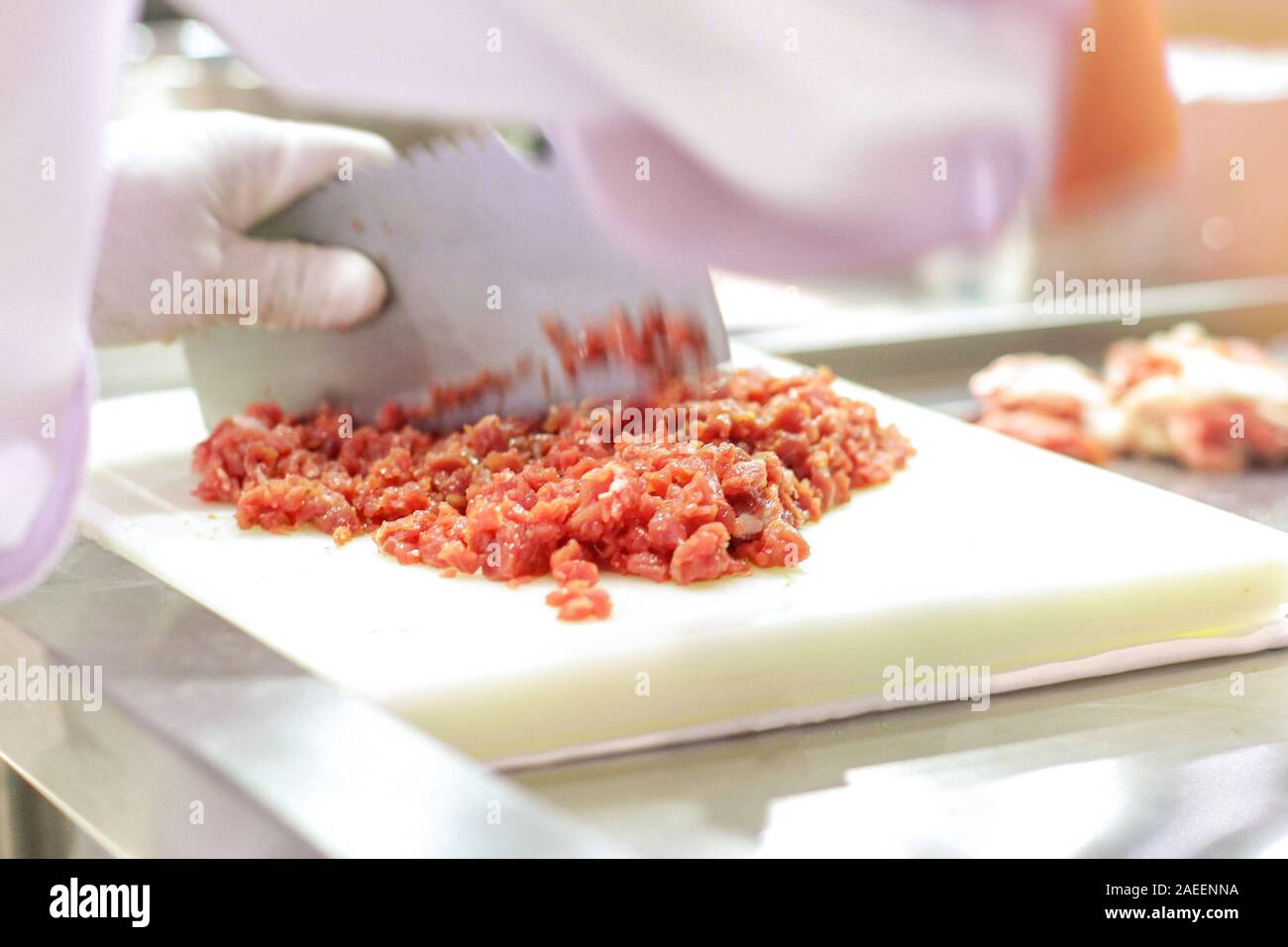 Chef is chopping the raw pork on cutting board with knife to cook in ...