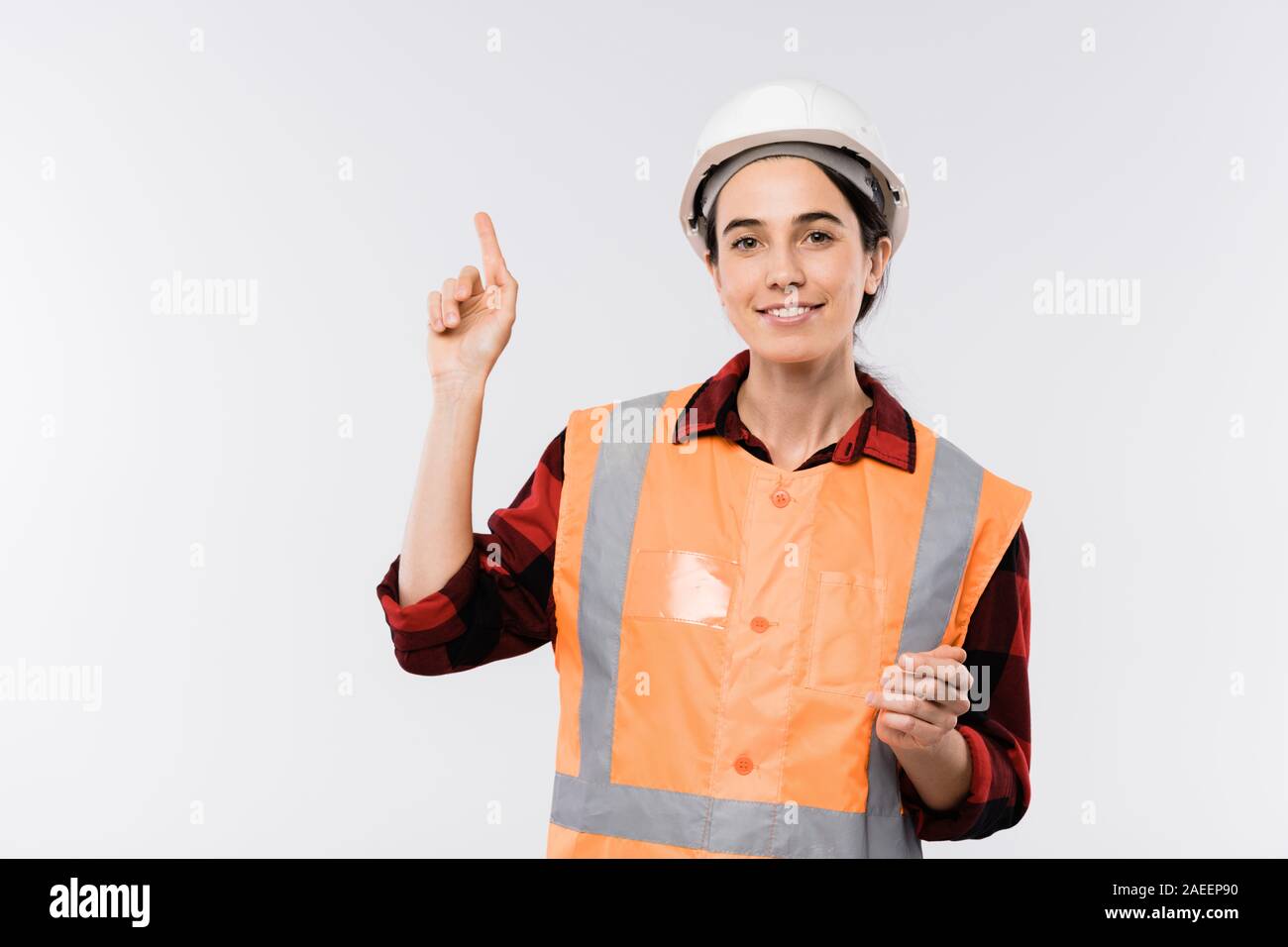 Pretty young female engineer in helmet and orange jacket pointing ...