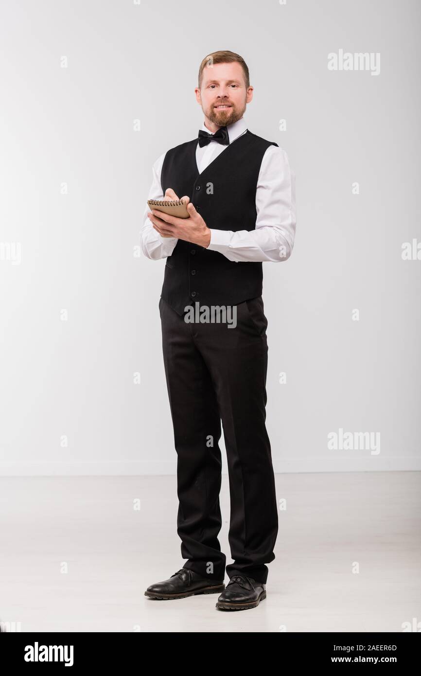 Young elegant waiter with notepad and pen writing down order of one of ...
