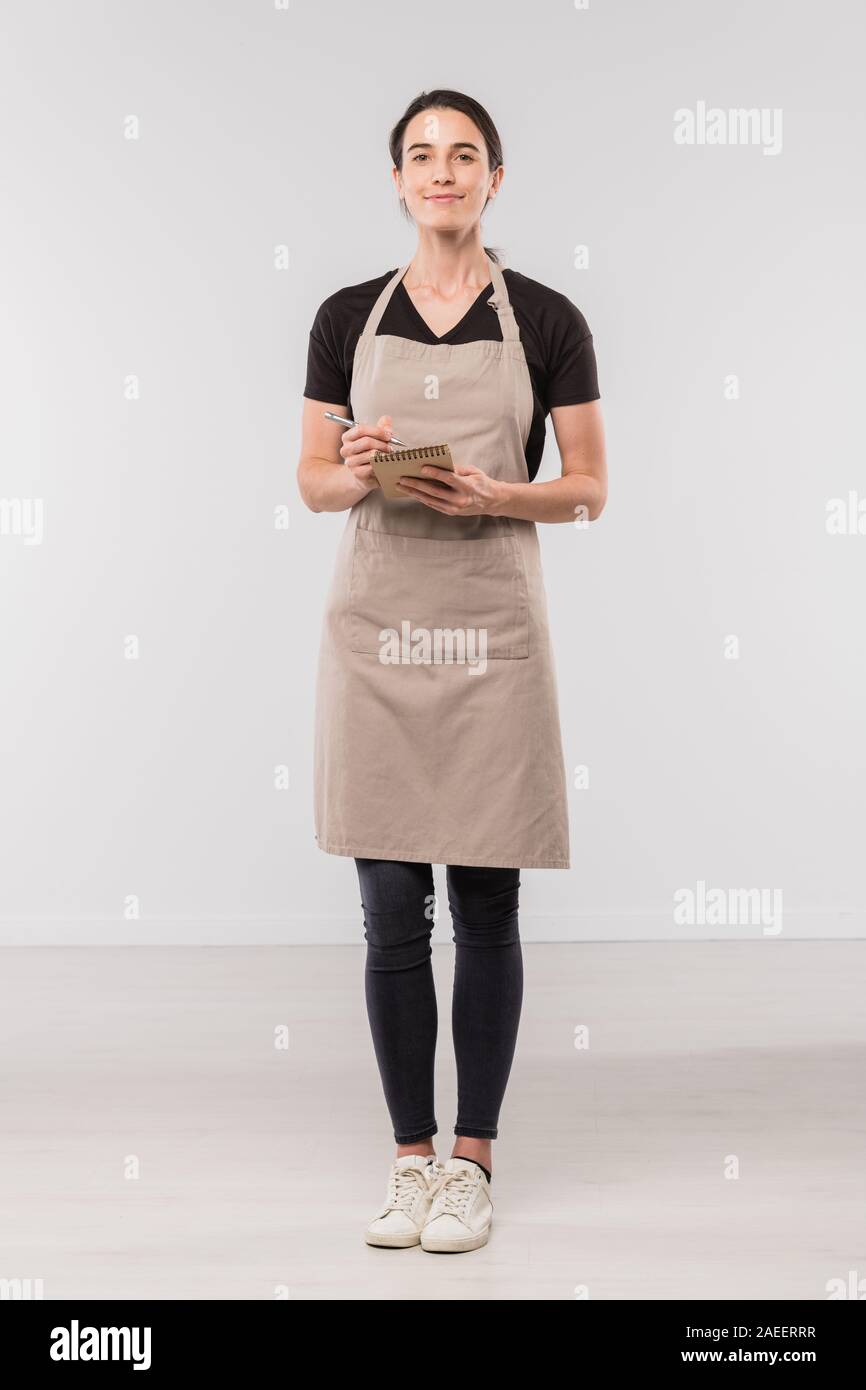 Pretty brunette waitress in workwear making notes in small notepad ...