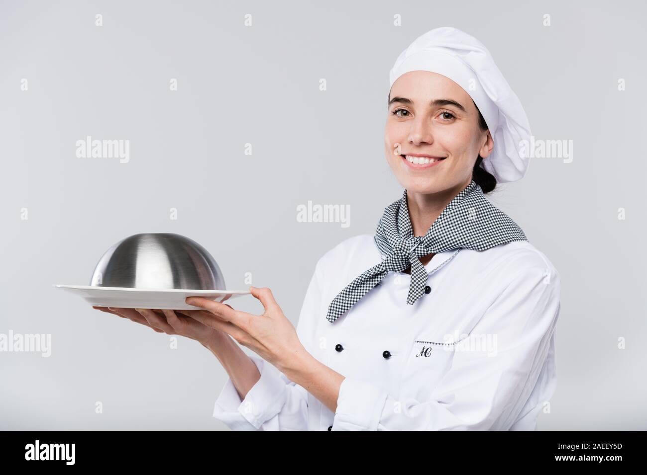 Young smiling female chef in uniform looking at you while carrying ...