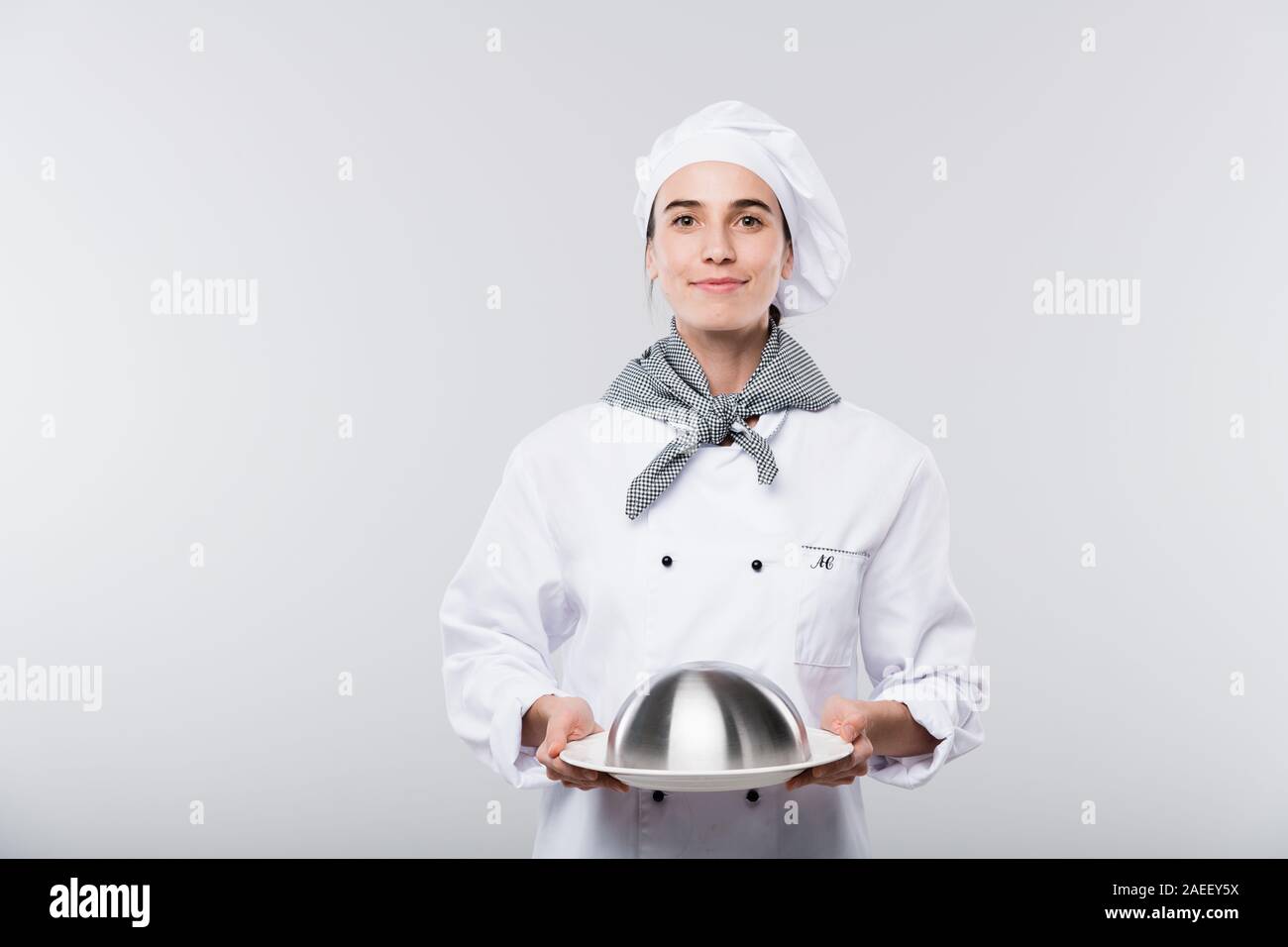 Happy young successful female chef in uniform carrying cloche with ...