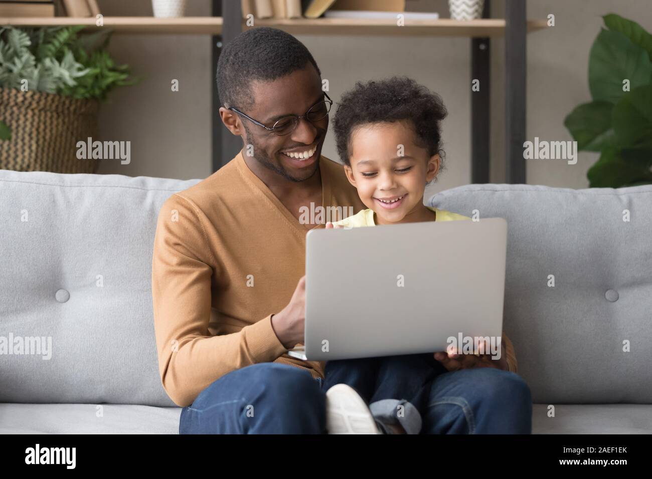 Smiling black dad and little son play computer game Stock Photo - Alamy