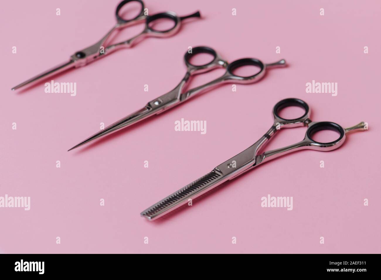 High angle photo of three pairs of metalscissors lined up row over pink ...