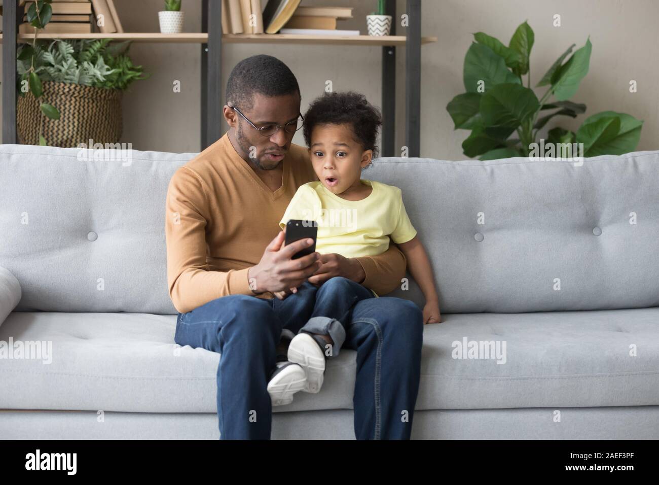 Surprised black dad and son watch video on smartphone Stock Photo - Alamy