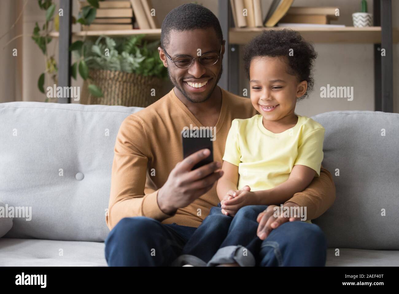 Smiling black father and son watch video on smartphone Stock Photo - Alamy