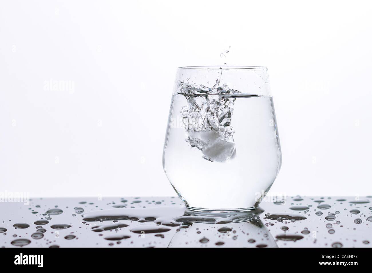 cubes of ice dropping in a glass of water with splashes and drops on a ...