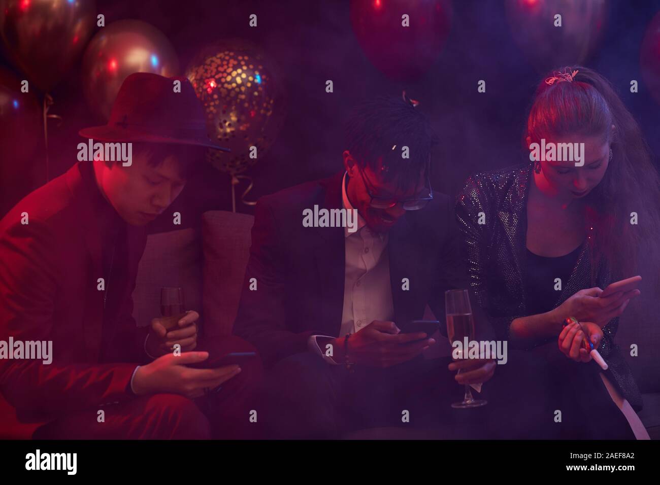 Group of trendy young people using smartphones during party in smoky ...