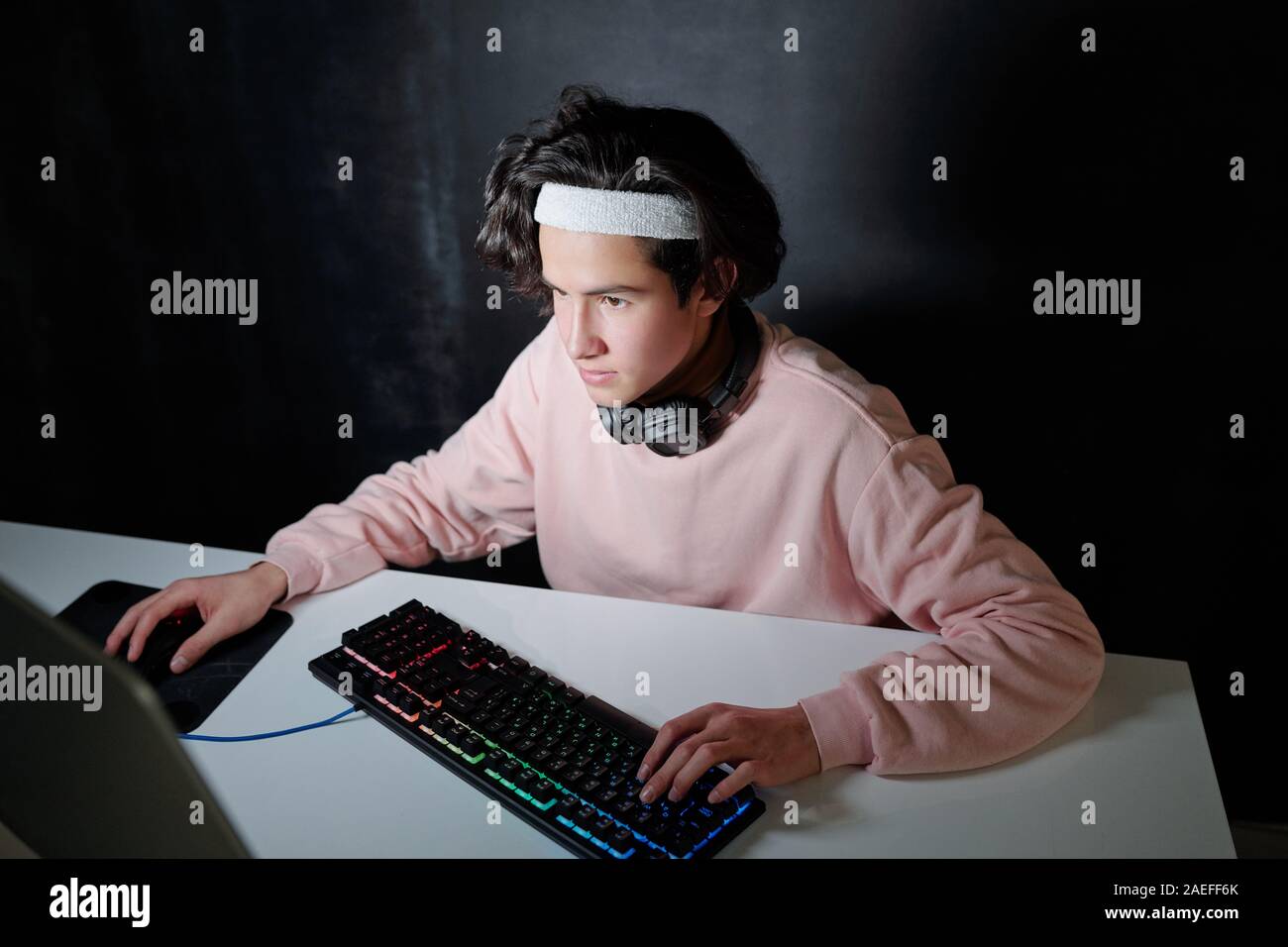 Young serious man in casualwear sitting by desk in front of computer ...