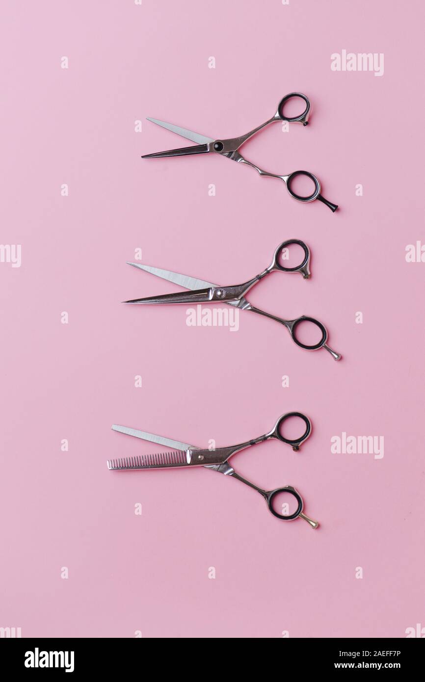Three pairs of metal hairdresser scissors in a vertical row over pink ...