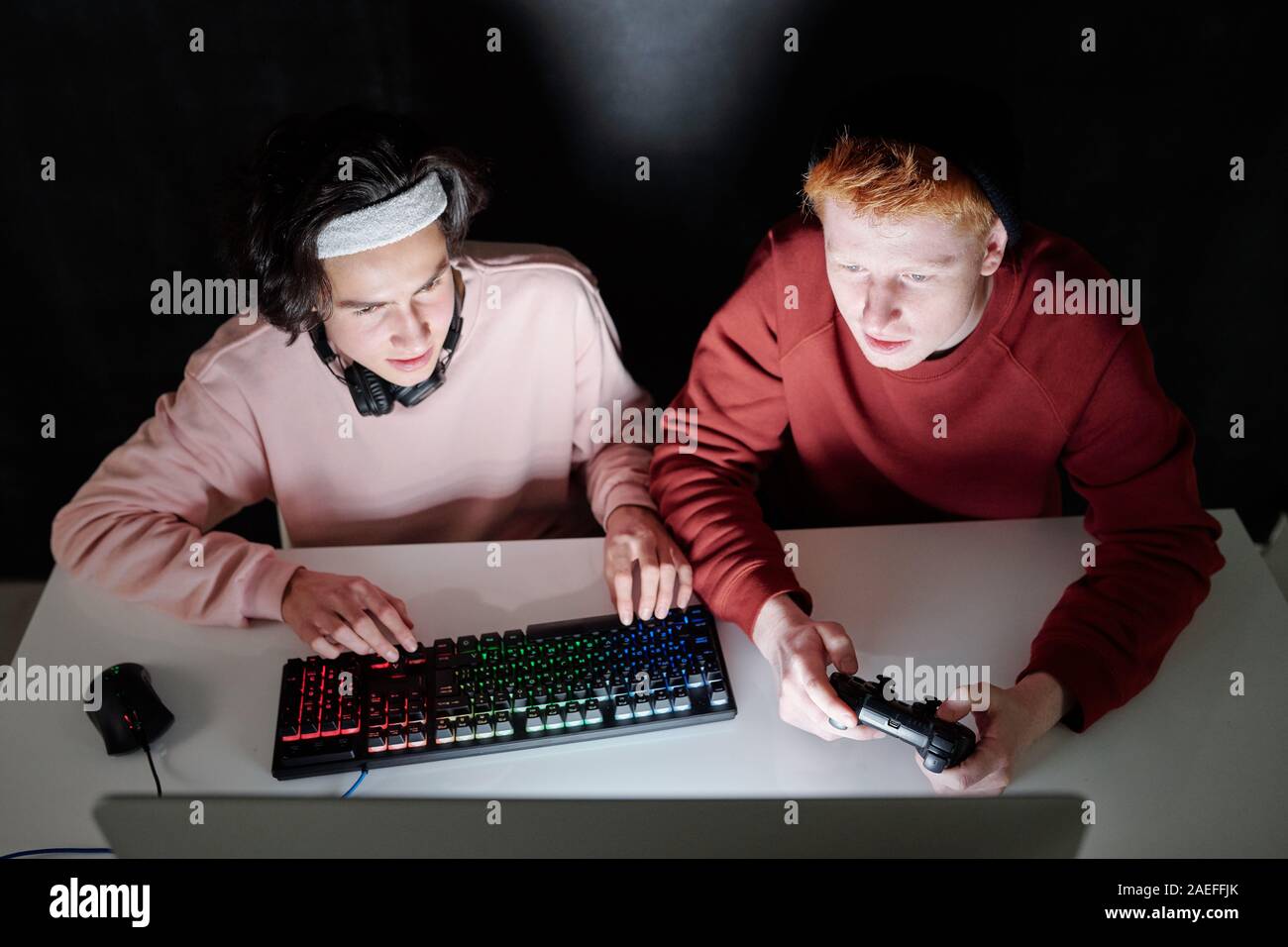 Two friendly guys in casualwear playing computer games while sitting by ...