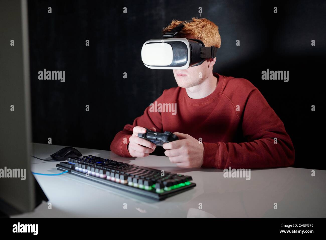 Young man with gamepad in vr headset sitting in front of computer ...