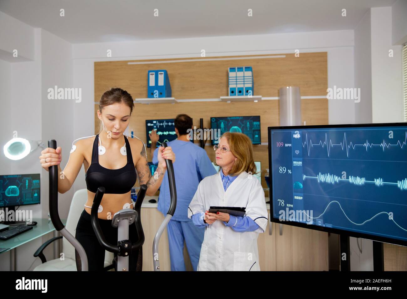 Female athlete doing physical effort on stepper and doctor with tablet ...