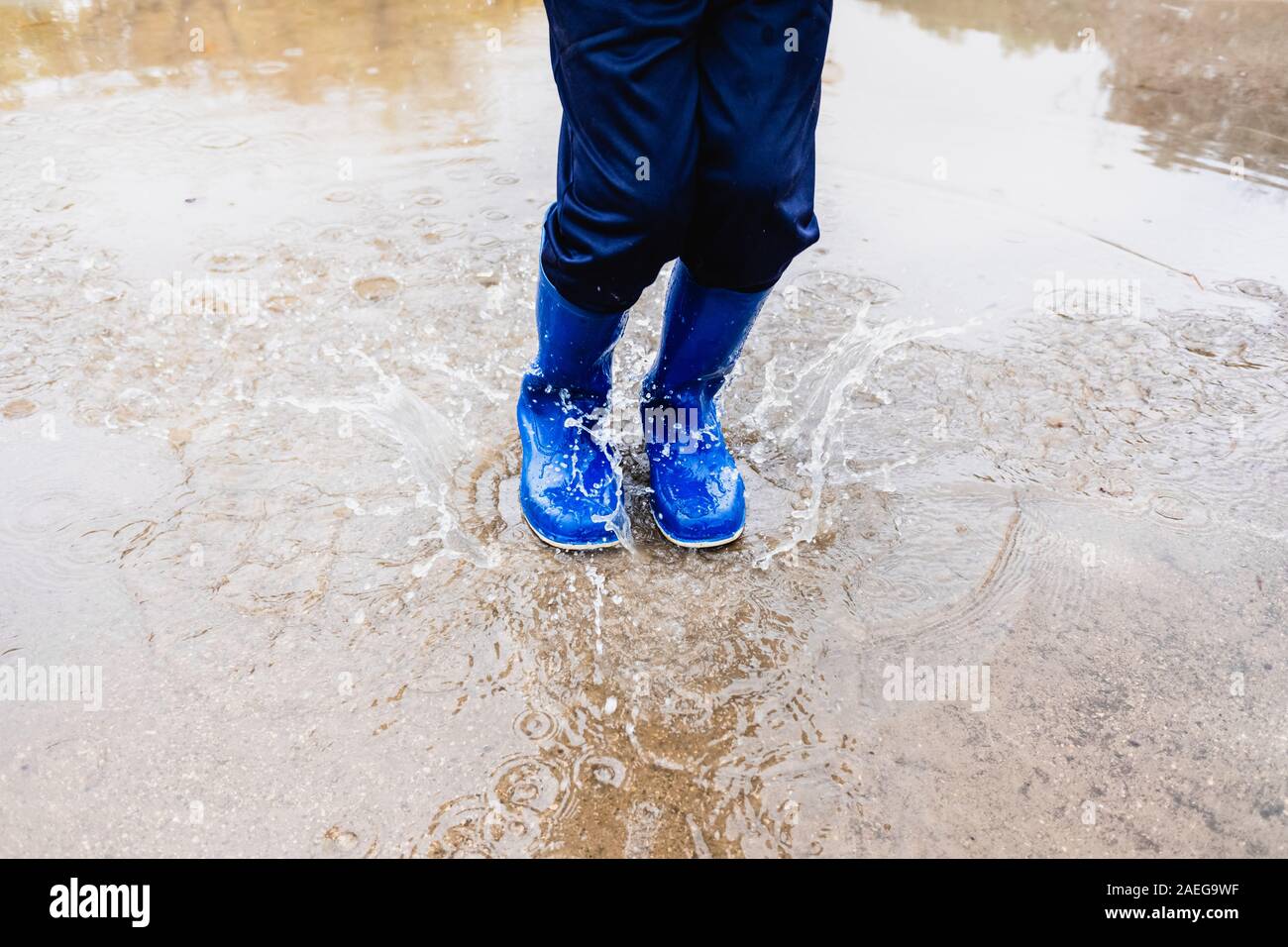 Boy with blue water boots jumps in a puddle Stock Photo - Alamy