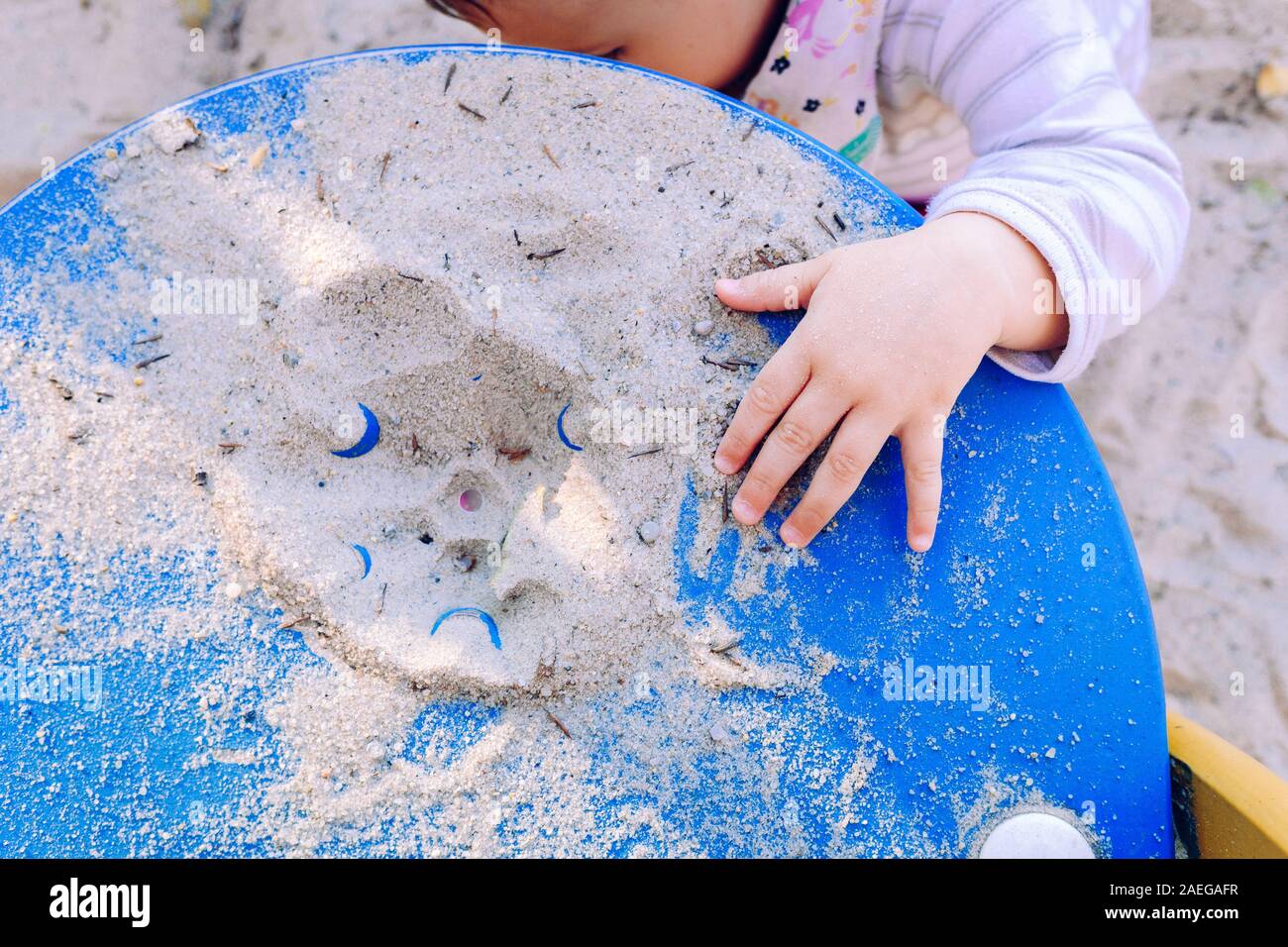 A baby play with sand in a sandpit, placing his hand to grab Stock ...
