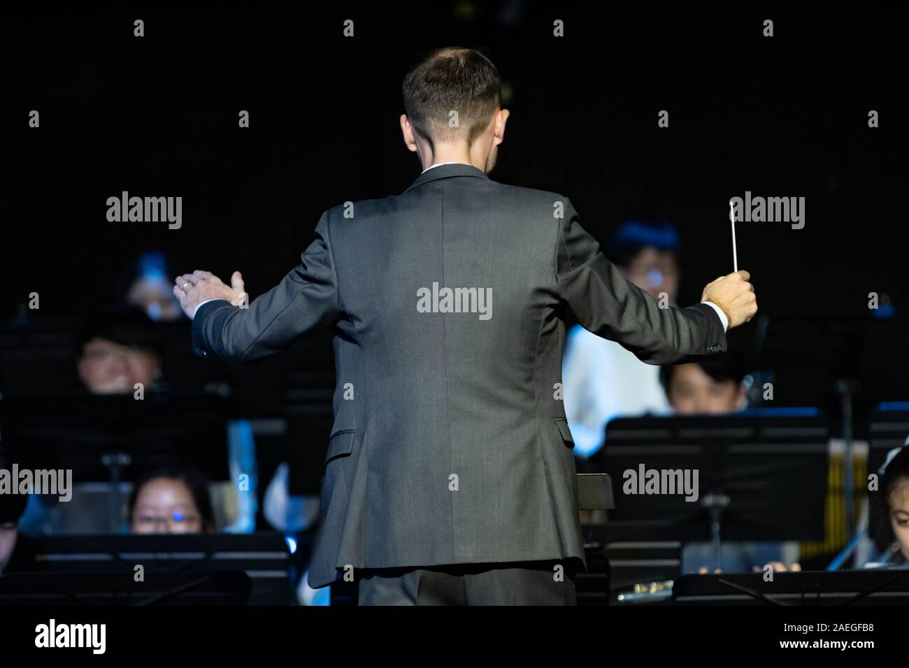 Back view of a male band conductor in formal suit conducting his ...
