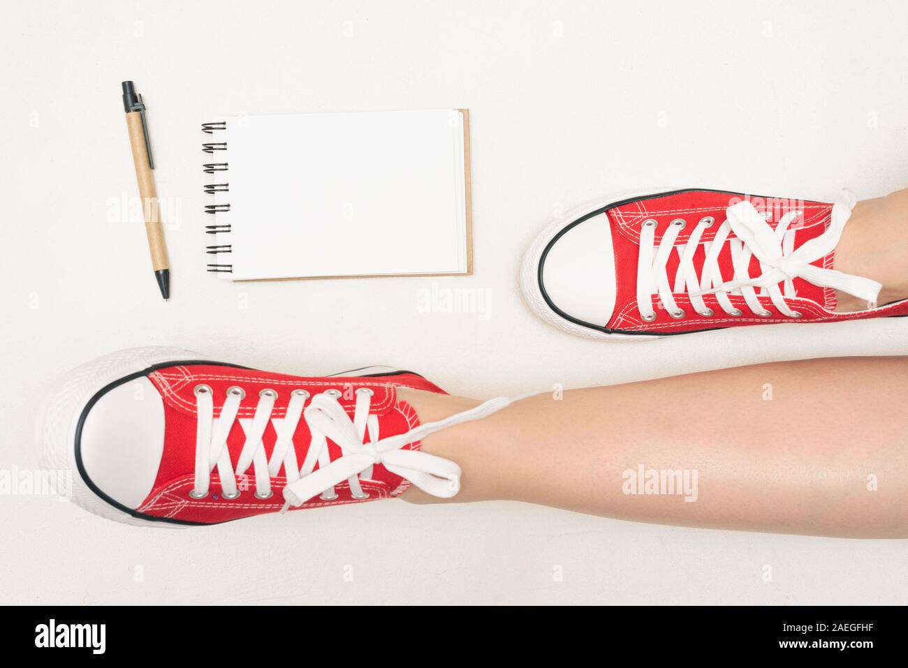 Red gumshoes on female legs and notepad with blank pages on white ...