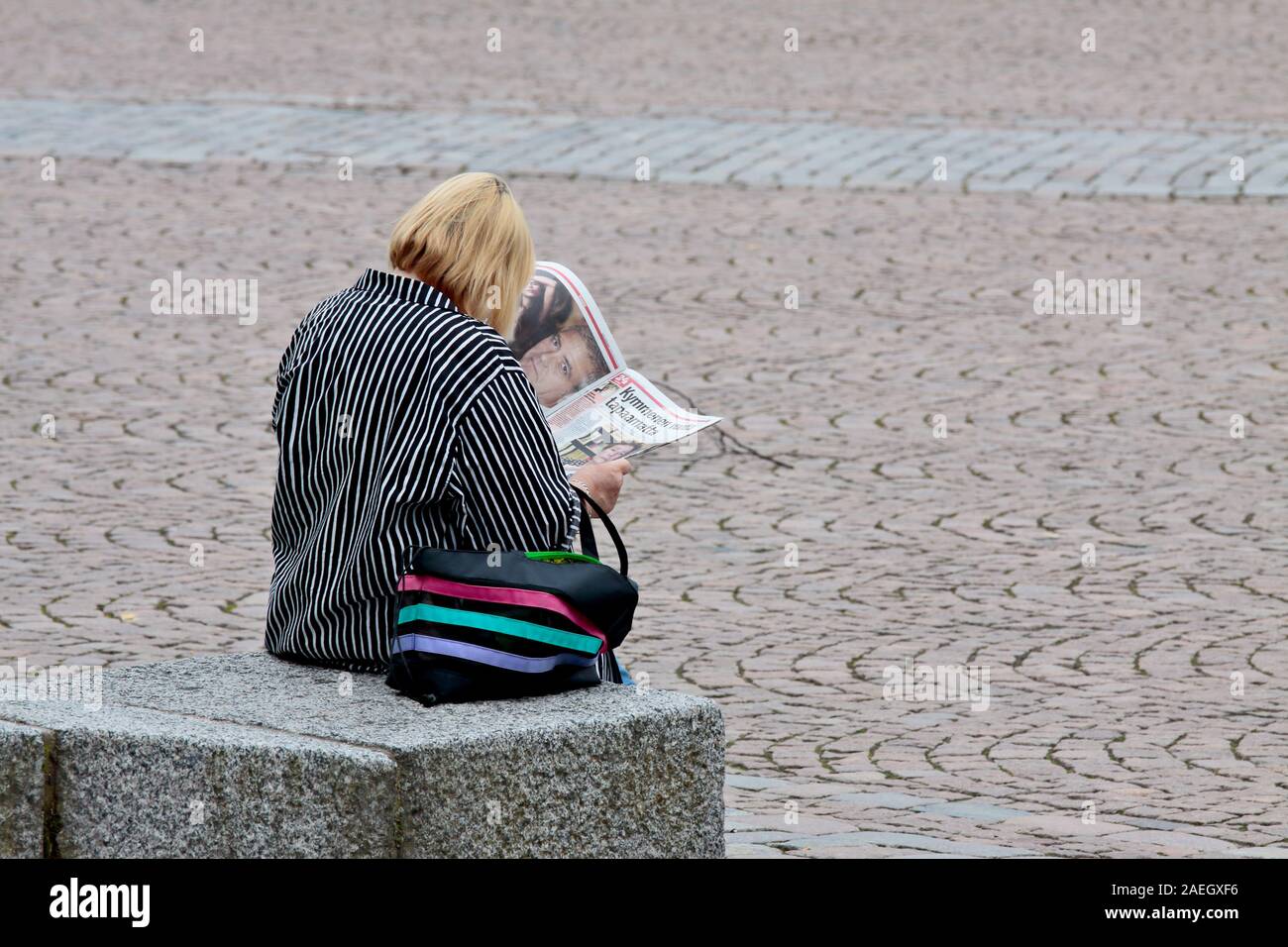 A woman sitting outdoors in market place reading newspaper Stock Photo ...