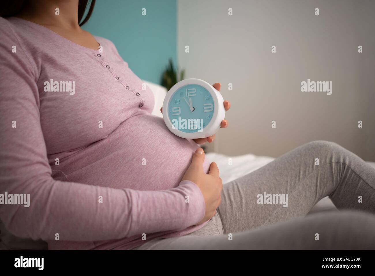 Pregnant woman holding her stomach and clock that shows five to twelve ...