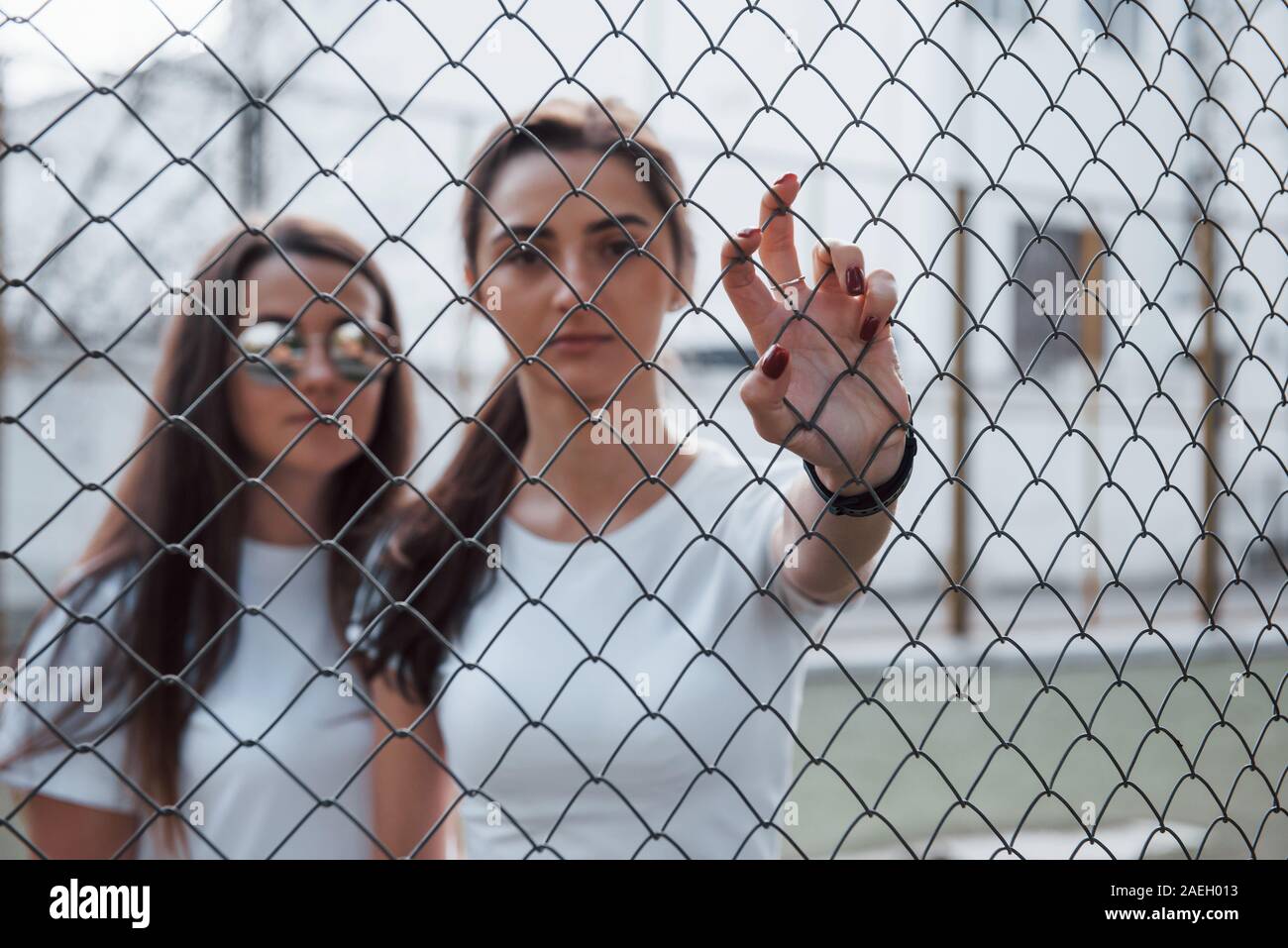 Modern youth. Two female friends stands behind the fence at daytime ...