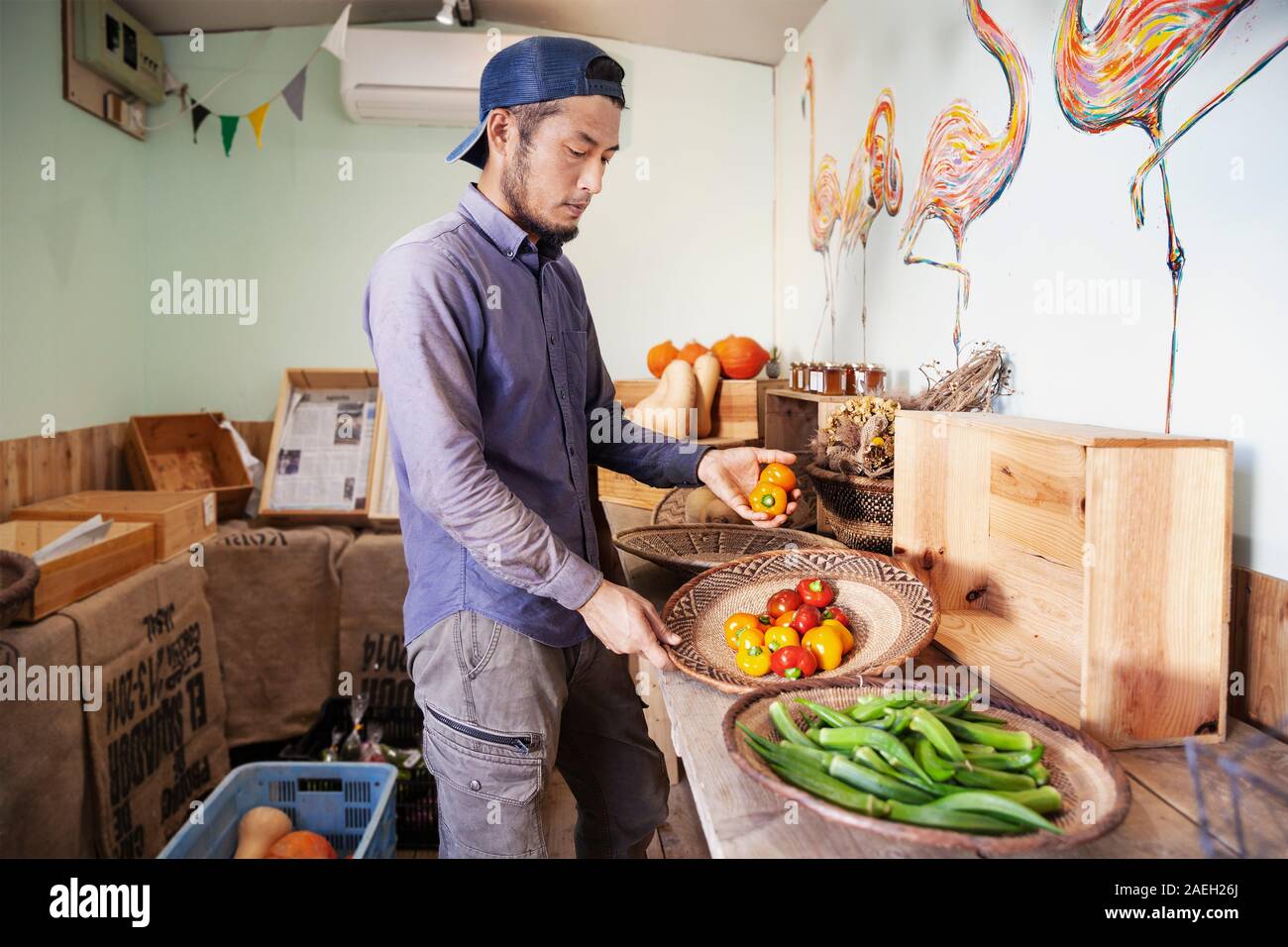 Japanese man wearing cap standing in farm shop, holding bowl with fresh ...