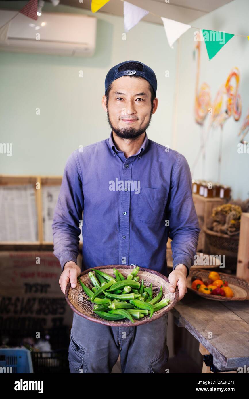 Smiling Japanese man wearing cap standing in farm shop, holding bowl ...