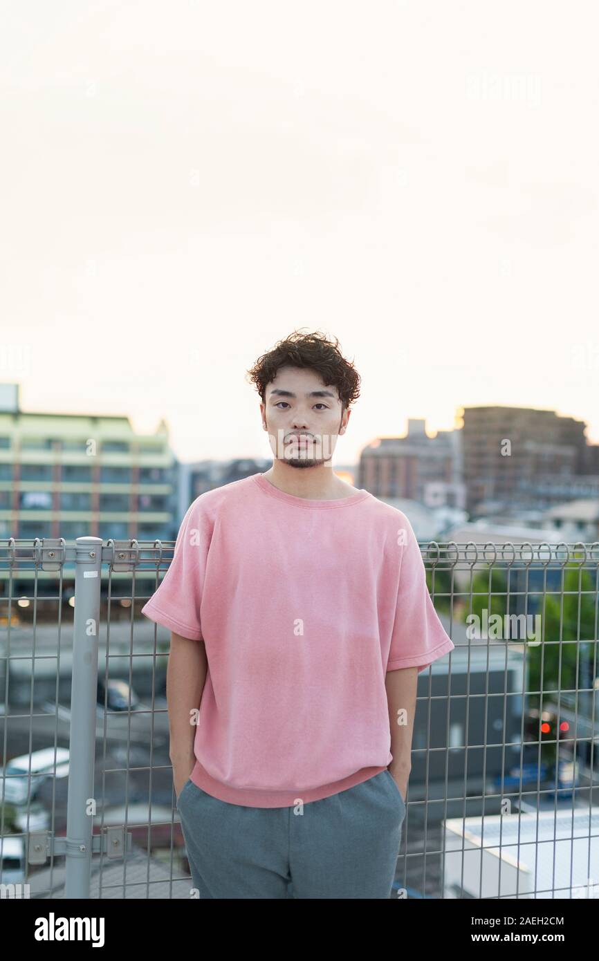Young Japanese man standing on a rooftop in an urban setting, looking ...
