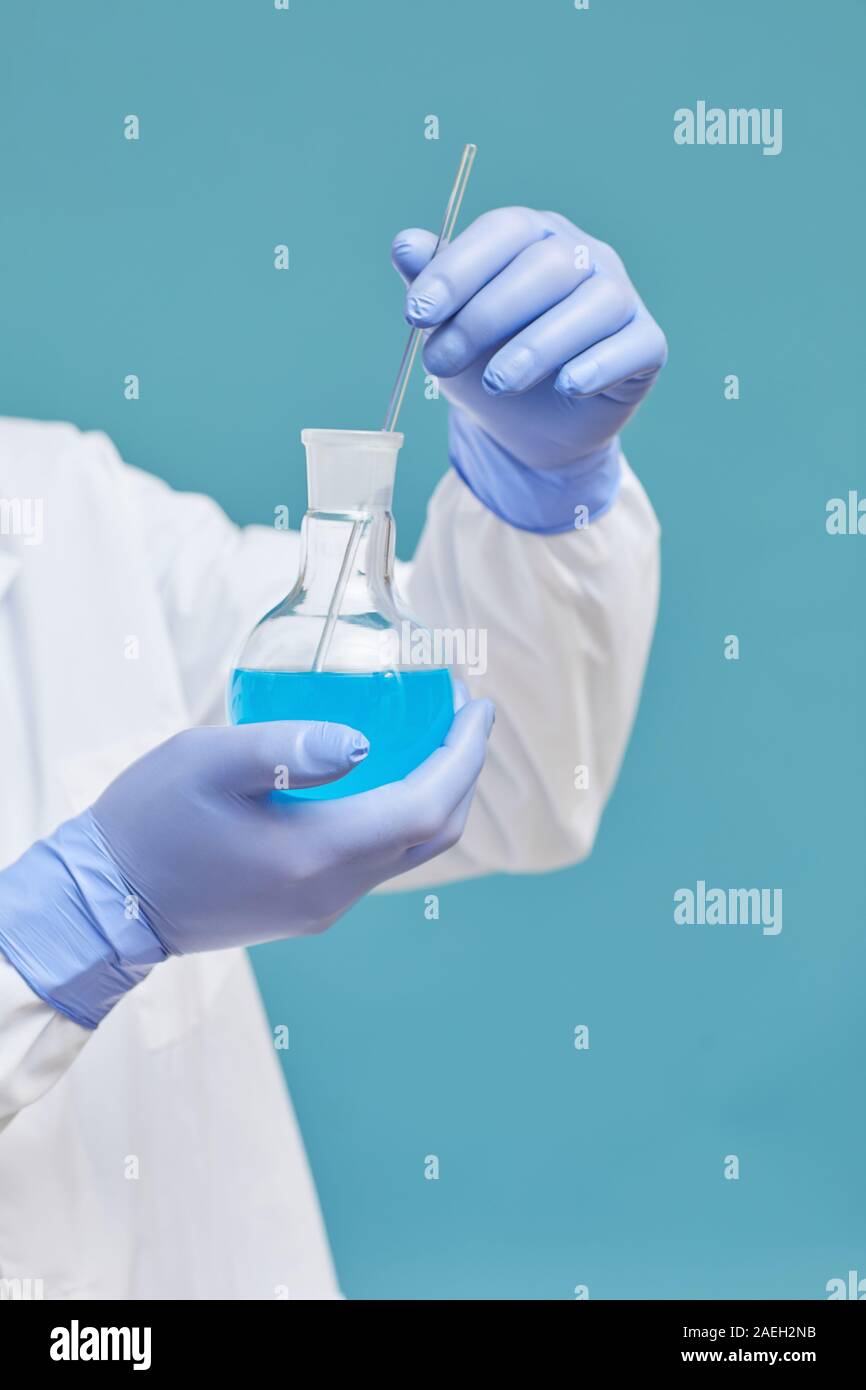 Close-up of scientist in gloves holding flask with blue liquid and ...