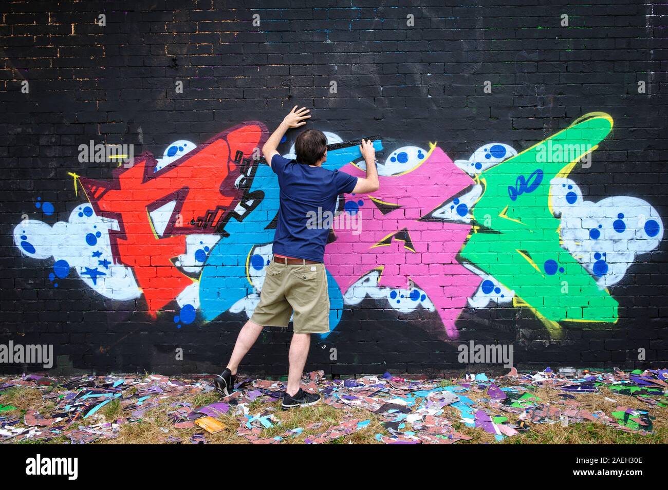 Male graffiti artist staying his own design onto a black wall Stock ...