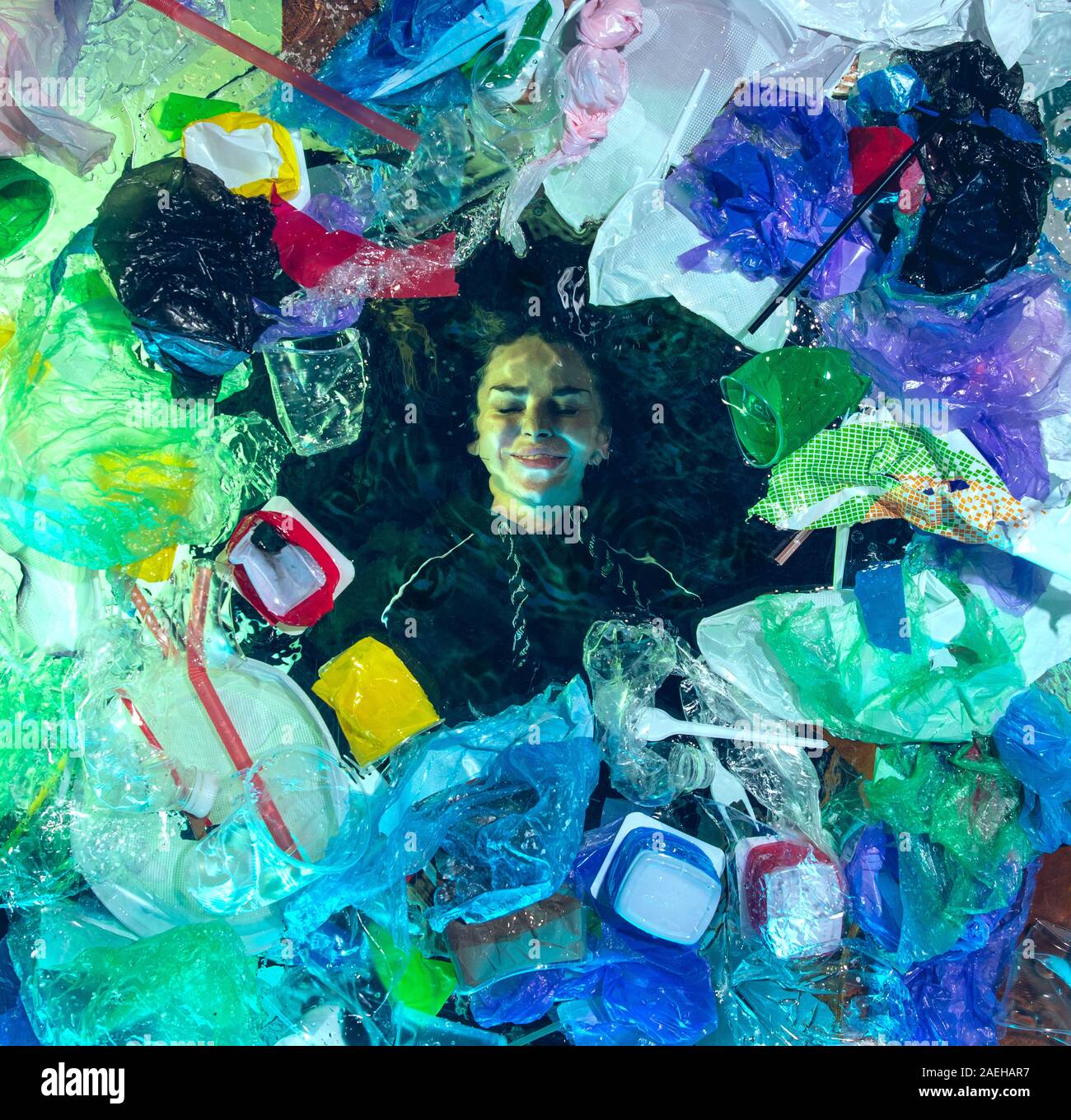 Woman drowning in water under plastic recipients pile, garbage. Used ...