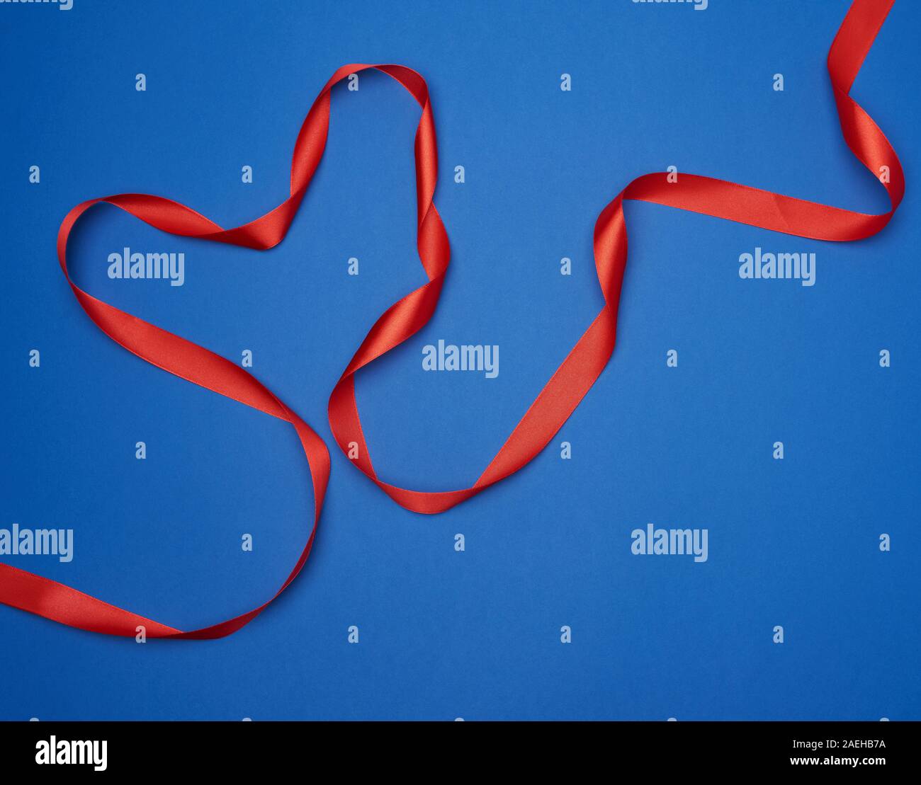 red silk thin ribbon twisted on a blue background, trendy classic color ...