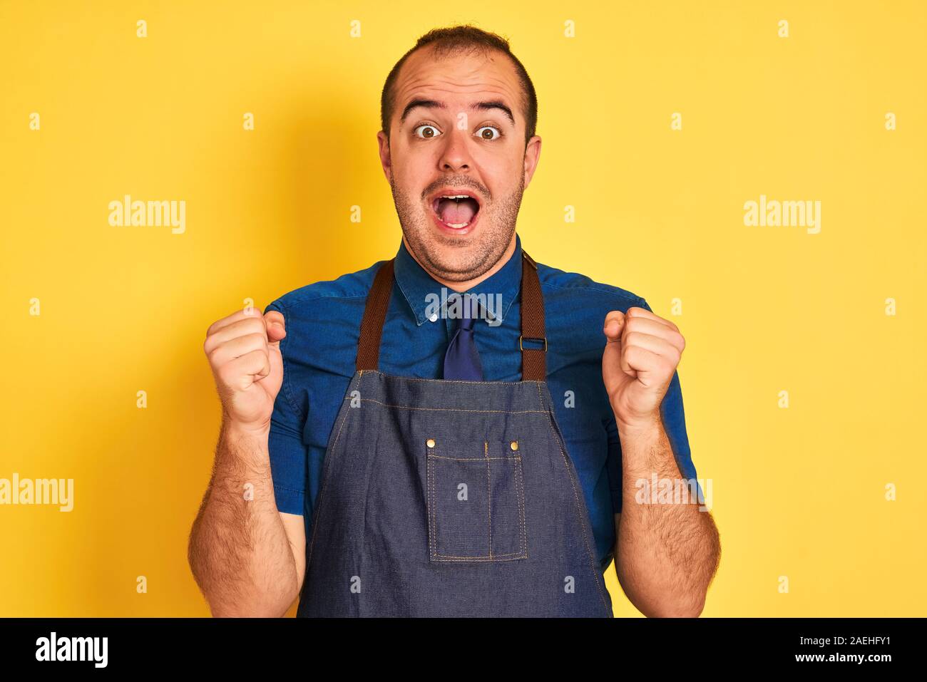 Young shopkeeper man wearing apron standing over isolated yellow ...