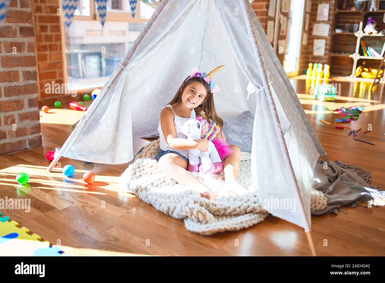 Adorable toddler sitting on the floor inside tipi around lots of toys ...
