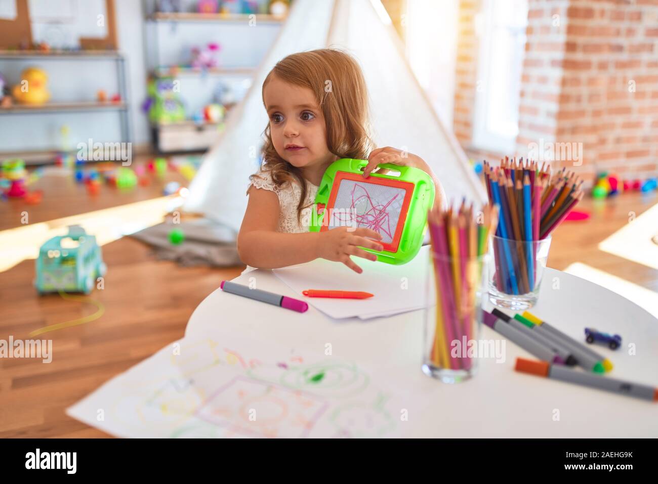Adorable blonde toddler drawing using digital board around lots of toys ...