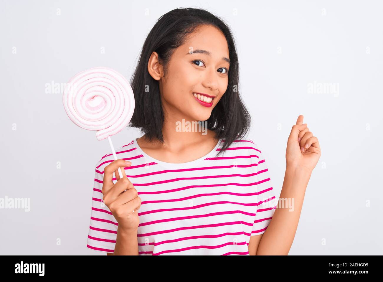Young beautiful chinese woman eating lollipop standing over isolated ...