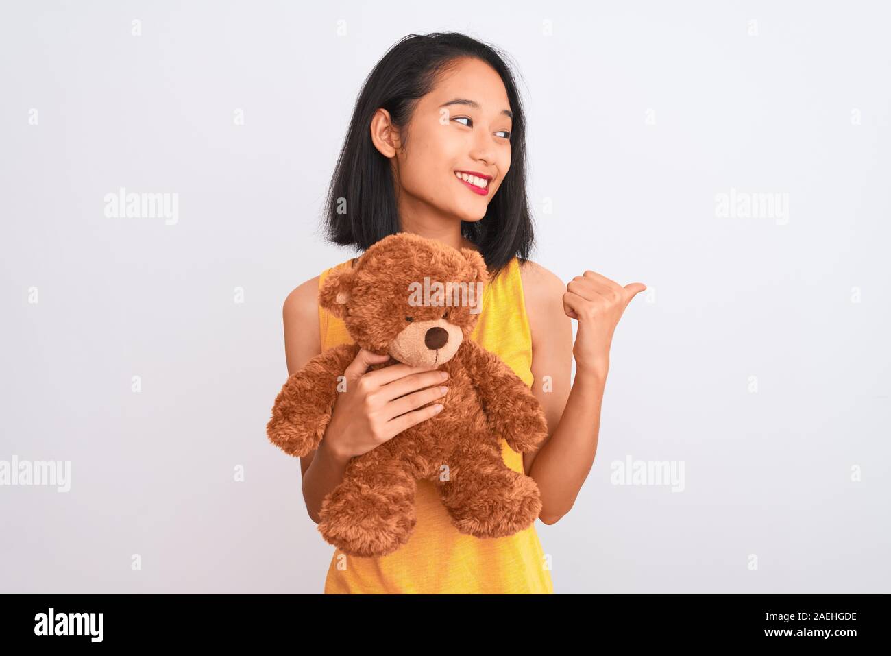 Young beautiful chinese woman holding teddy bear standing over isolated ...
