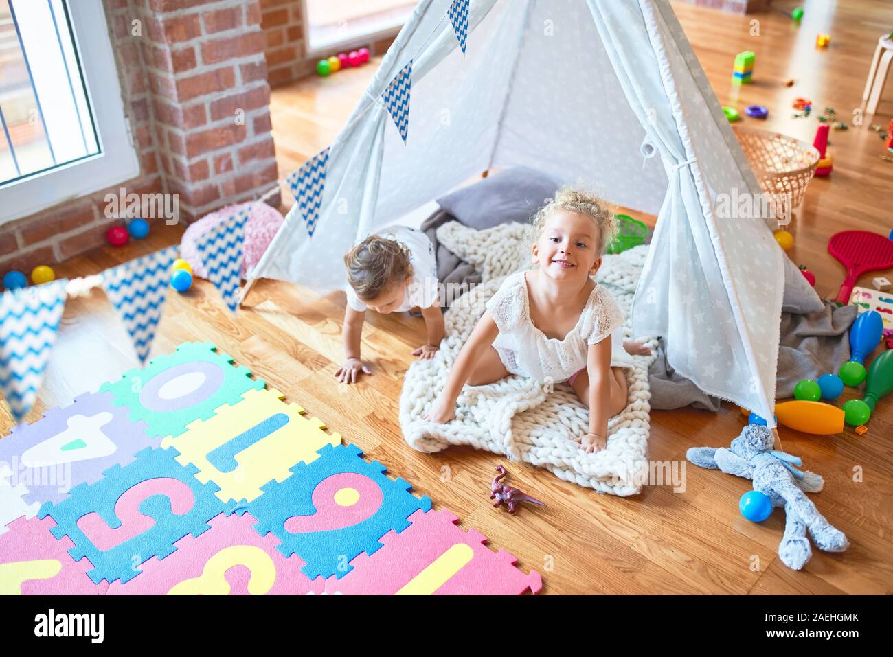 Beautiful toddlers playing inside tipi over blanket around lots of toys ...