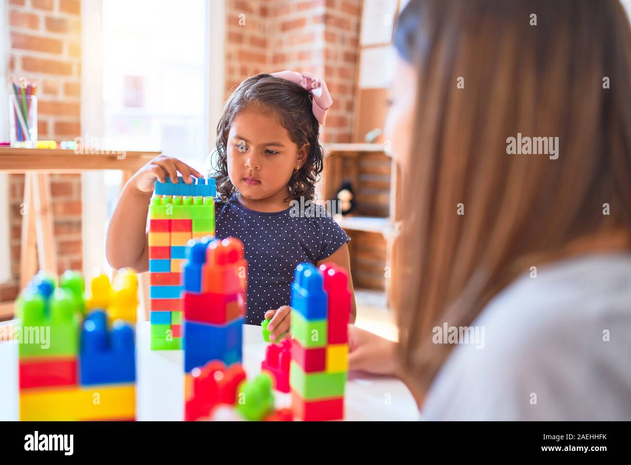 Beautiful teacher and toddler girl playing with construction blocks ...