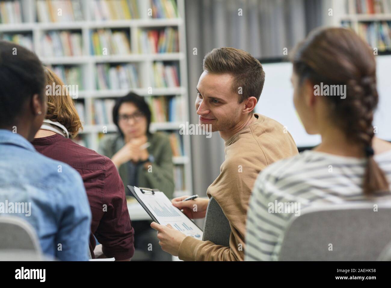 Young man with report talking to his colleagues during business ...